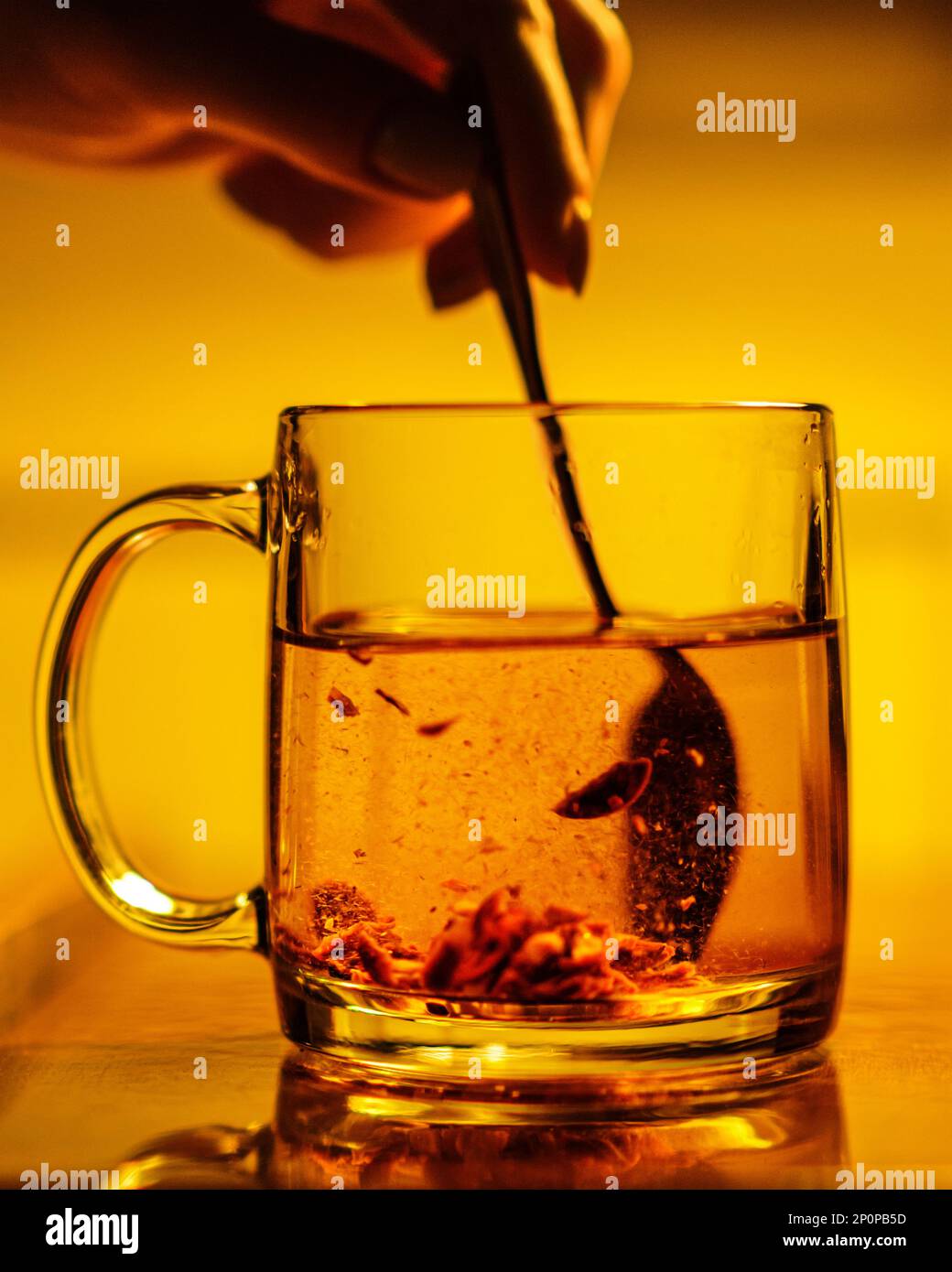 A glass mug with herbal tea on a table, woman's hand stirring it with a ...