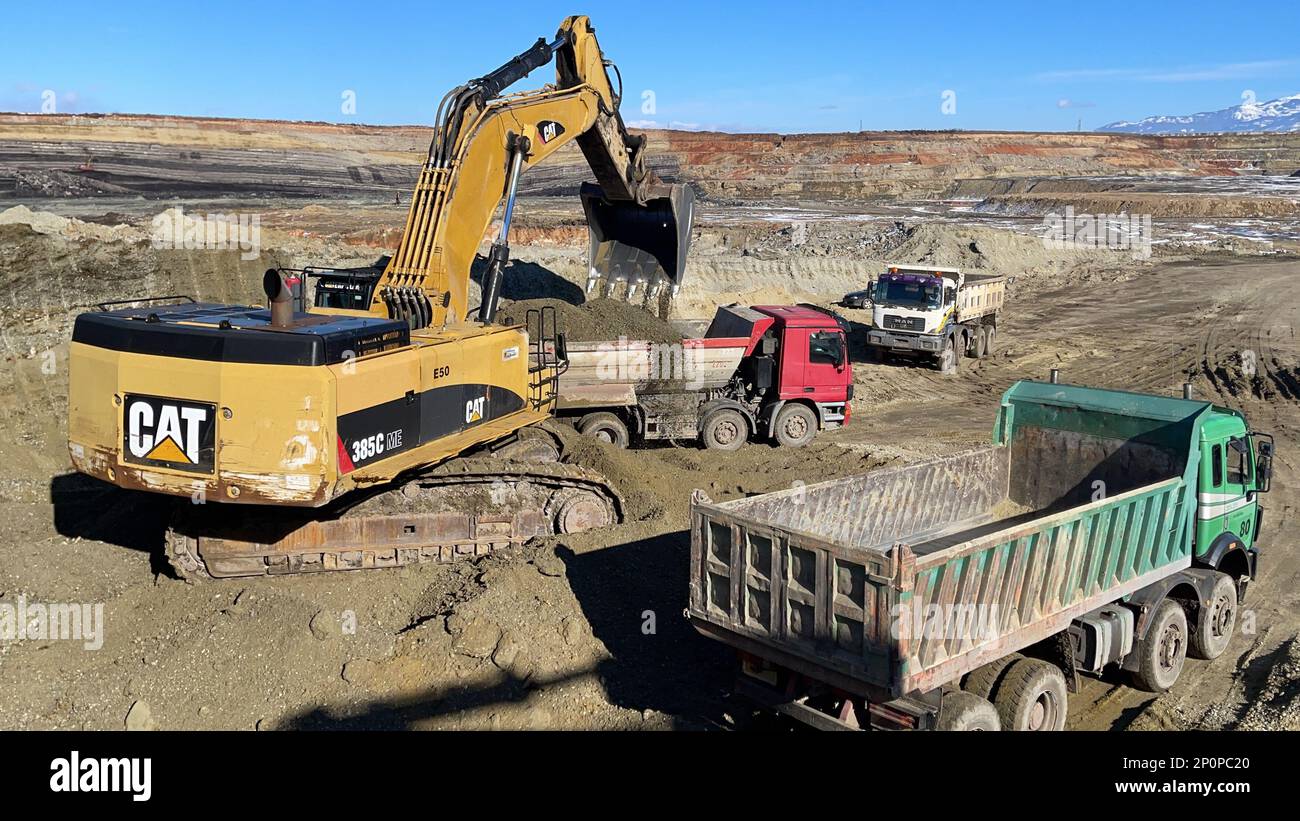 Excavator is loading continuously the trucks, working at a huge mining ...