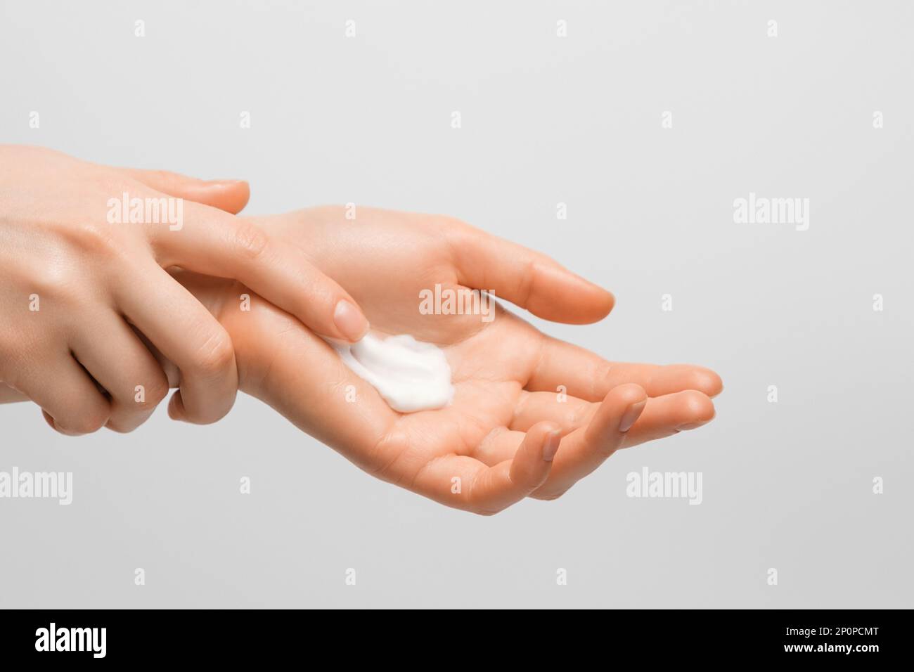 A girl smearing a handful of hand cream on her hand. Photo on gray ...
