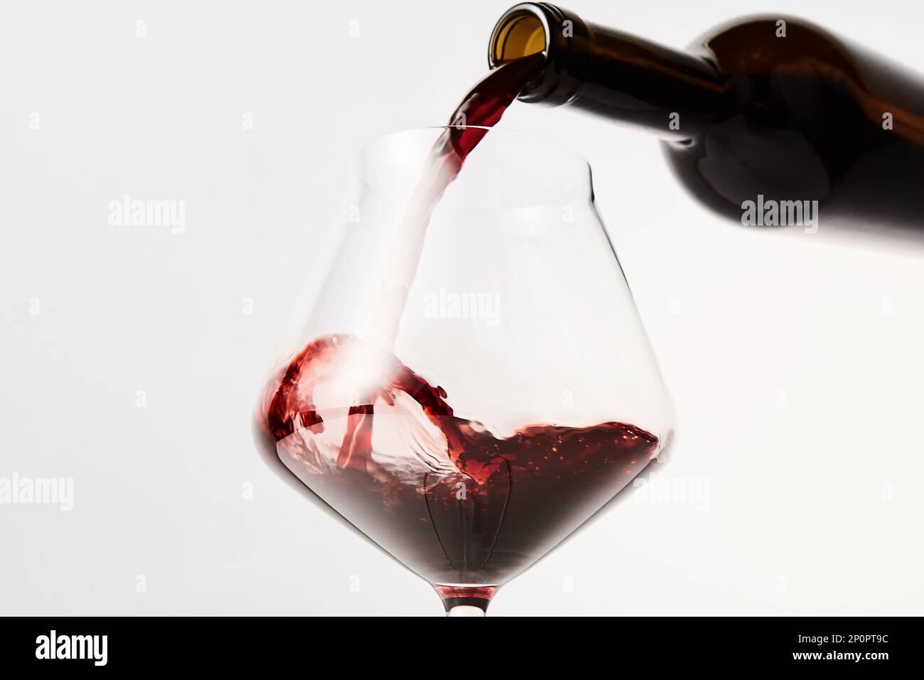 Red wine pouring into tilted wineglass from bottle Stock Photo - Alamy