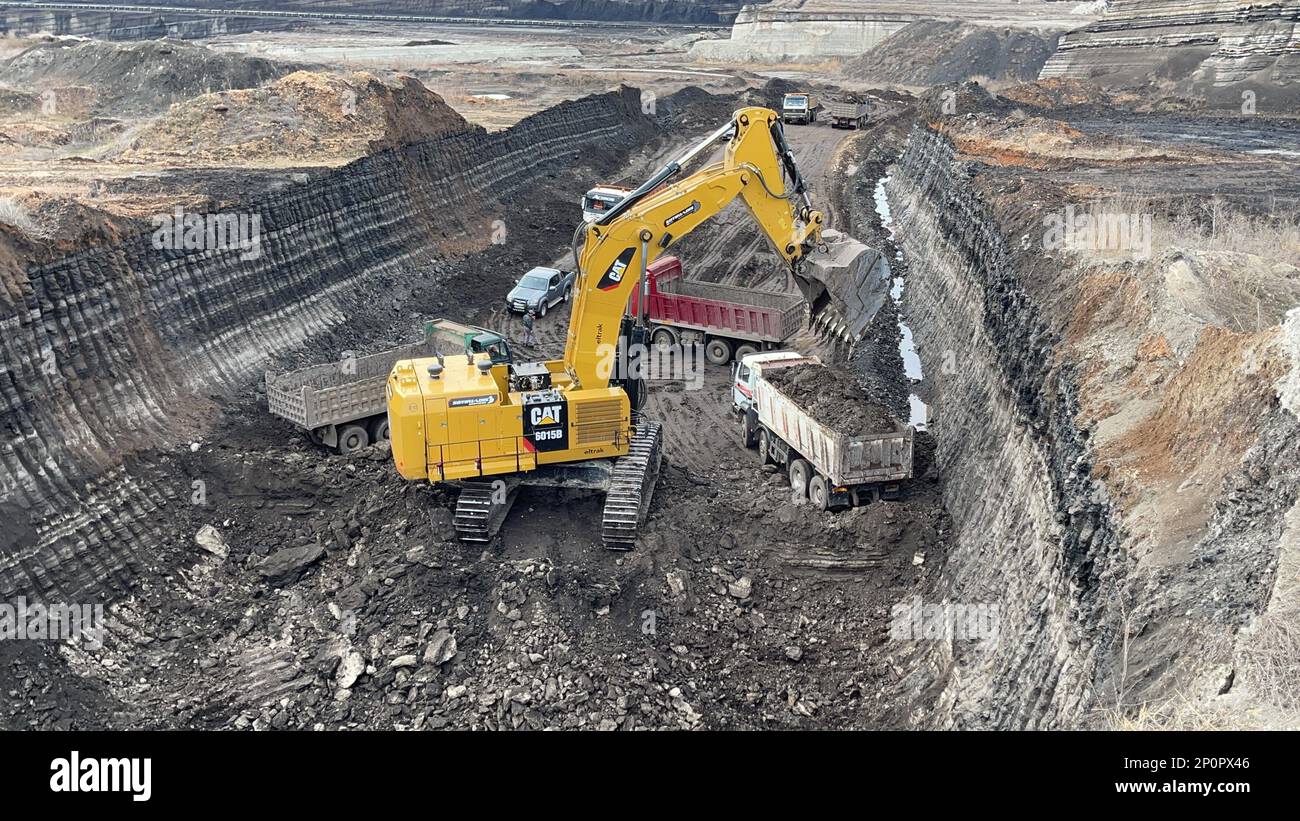 Excavator is loading continuously the trucks, working at a huge mining ...