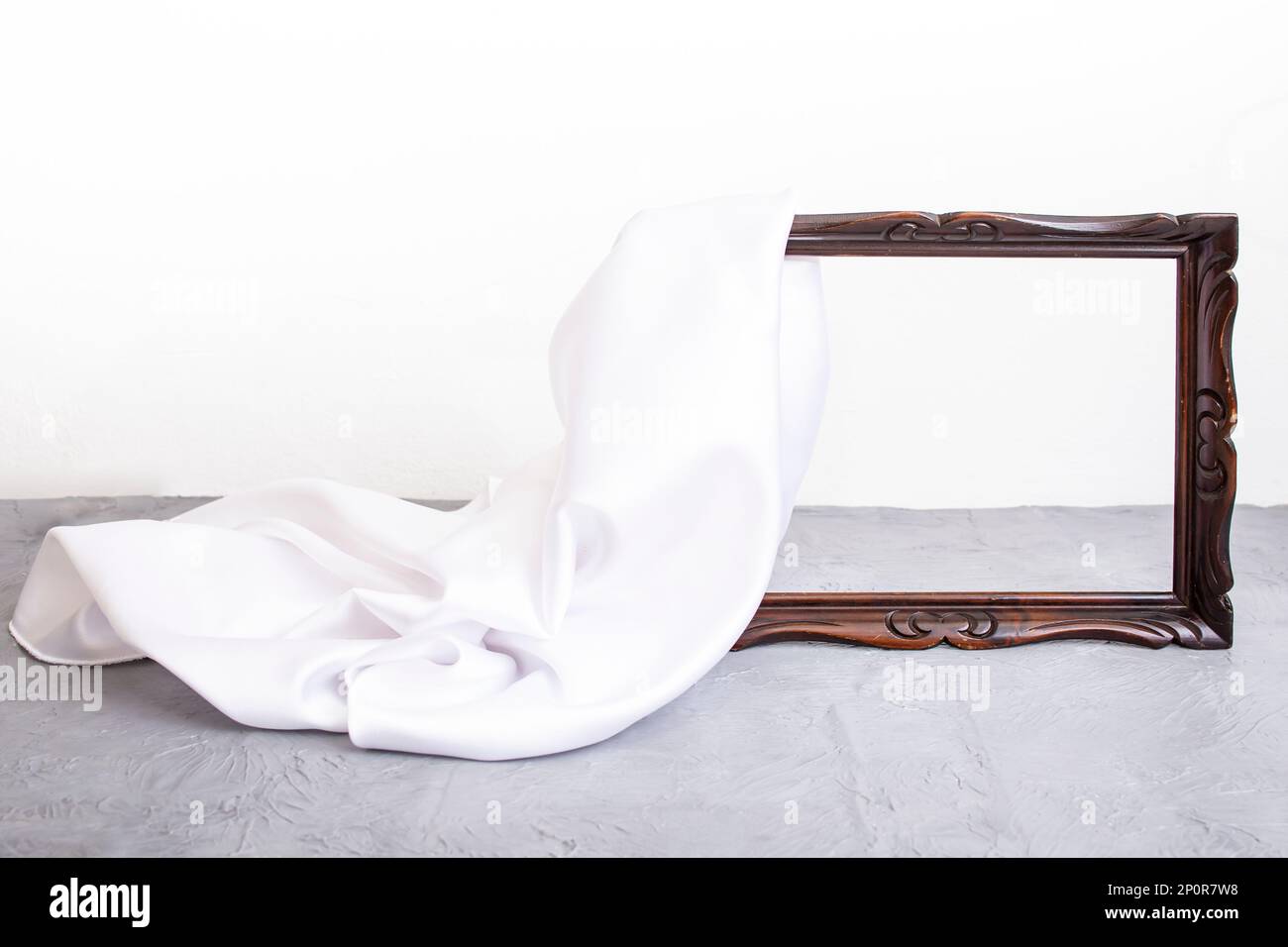 White satin unveiling a wooden frame on cement backdrop, product ...