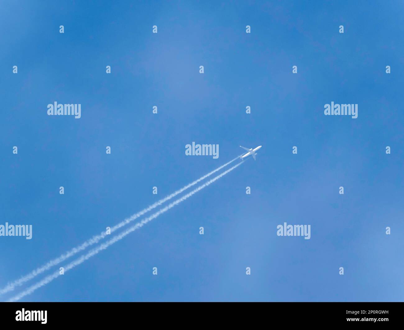 Passenger plane flies across clear blue sky leaving a jet contrail ...