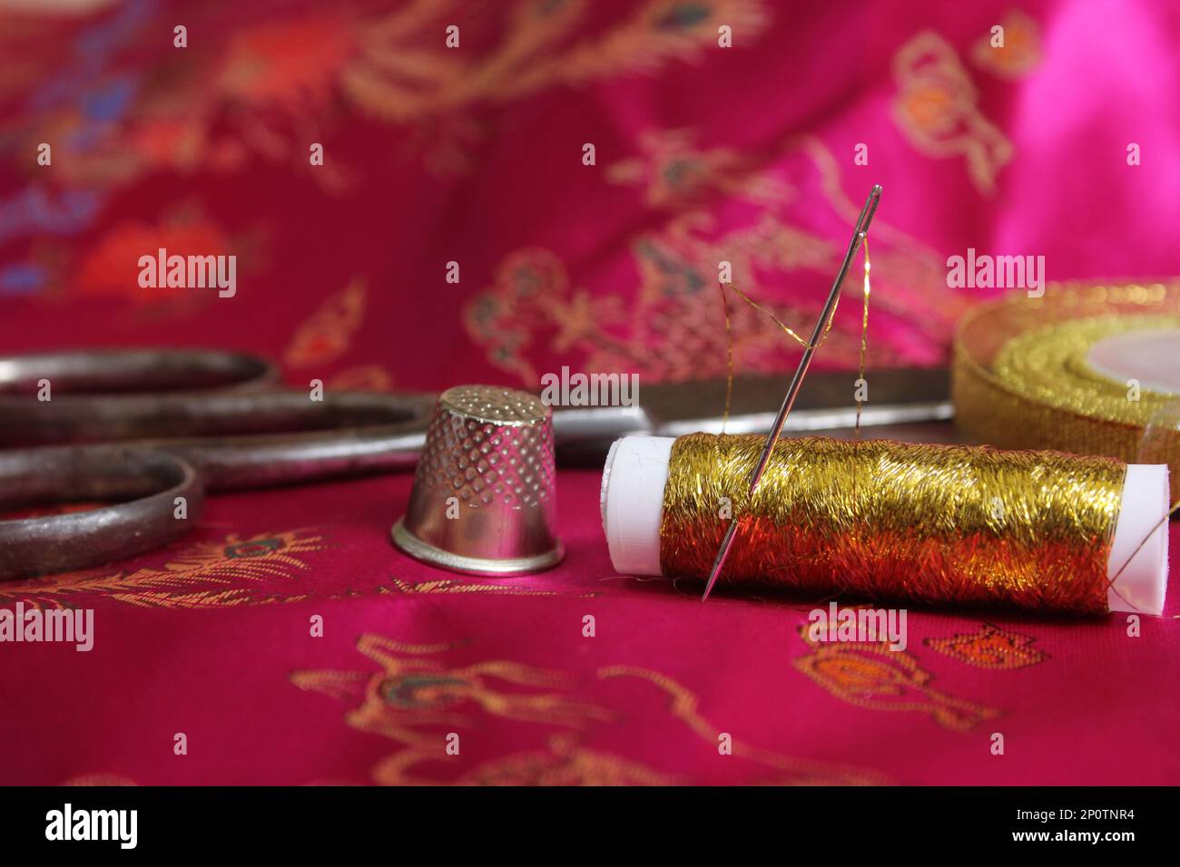 Spool of Gold Metallic Thread and Thimble on Vintage Pink Silk Fabric ...