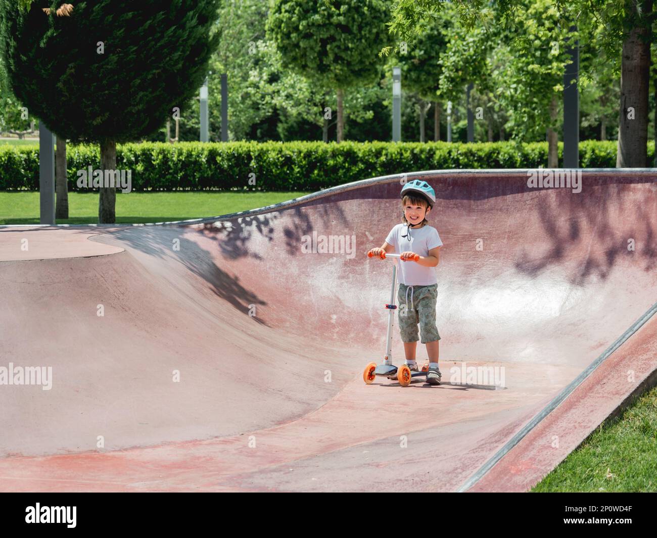 Little boy rides kick scooter in skate park. Special concrete bowl ...