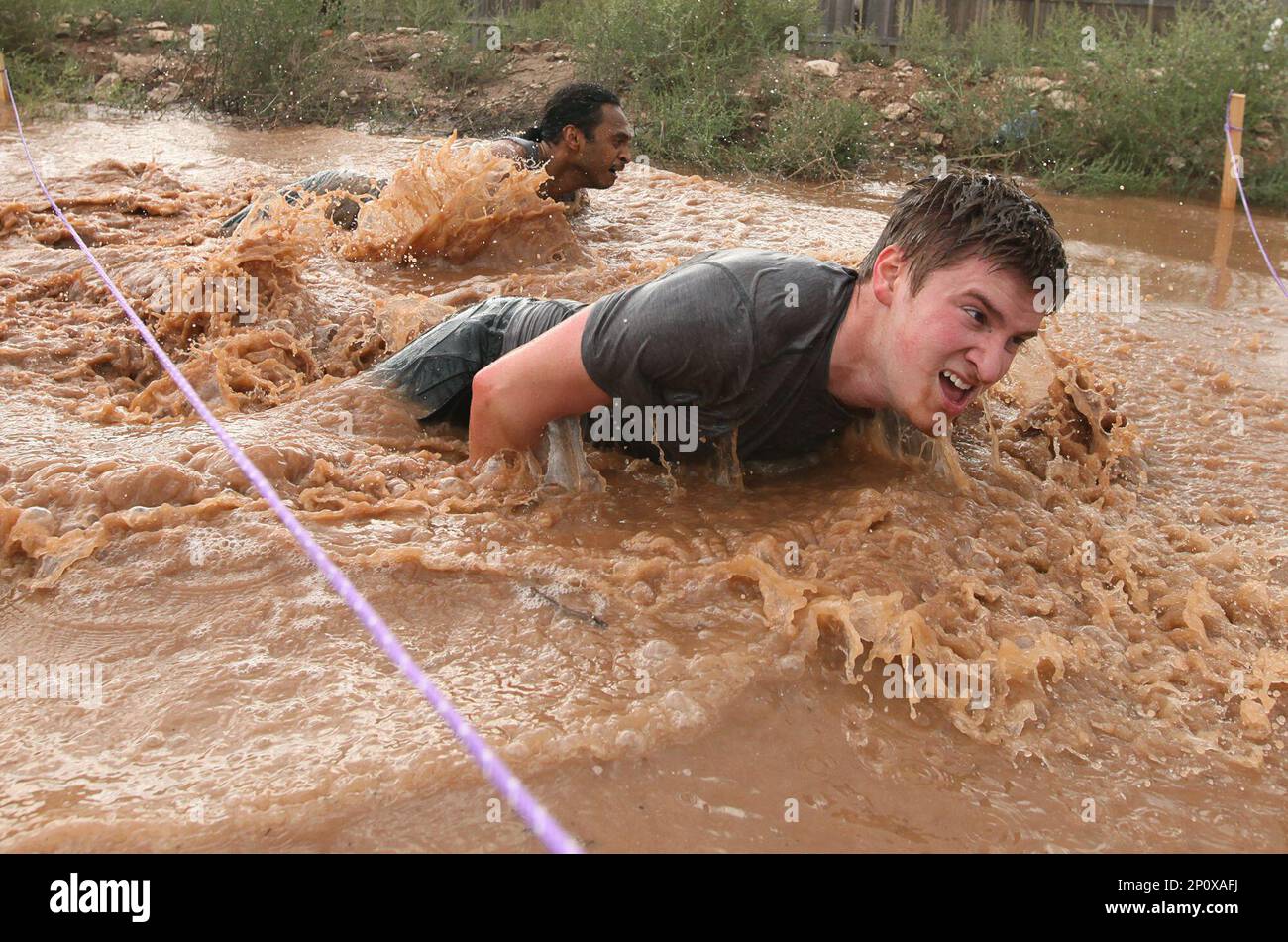 Two competitors crawl through mud during the first wave of runners at ...