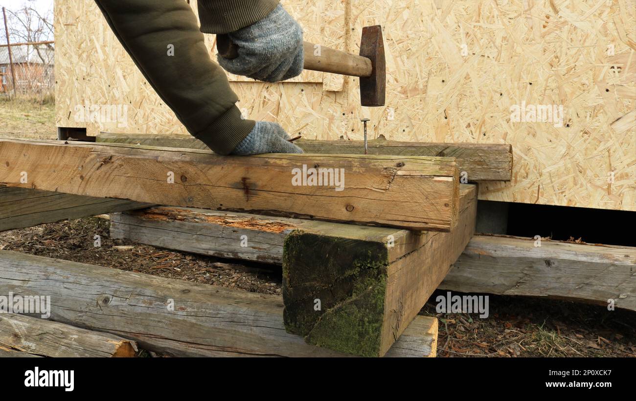 village builder hammering a long nail with a hammer into old boards ...