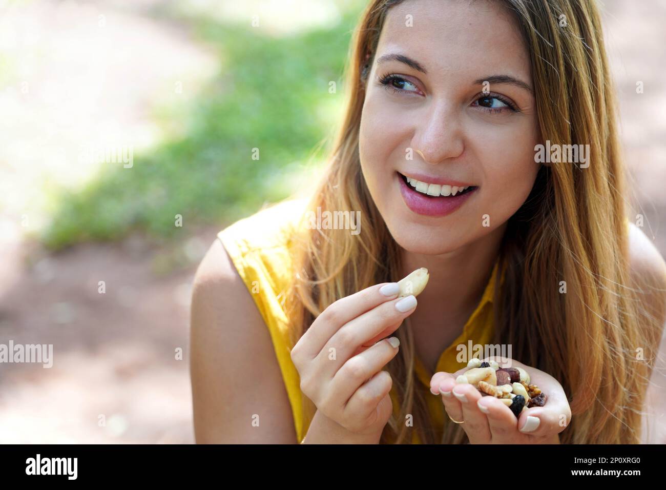 Close-up of healthy girl eating a mix of nuts seed dried fruits looking ...