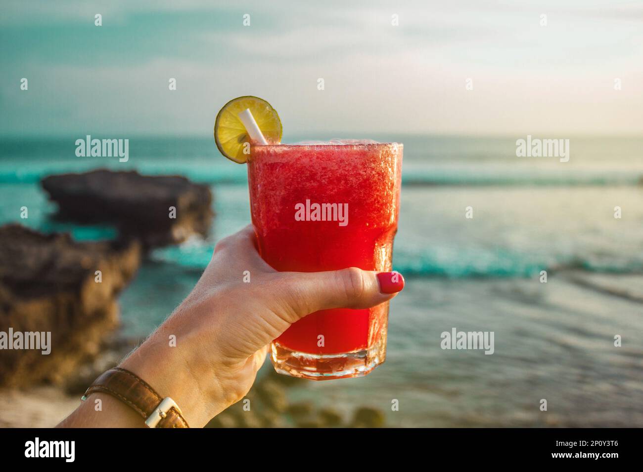 Hand with watermelon juice cocktail on the ocean background. Sunset on ...