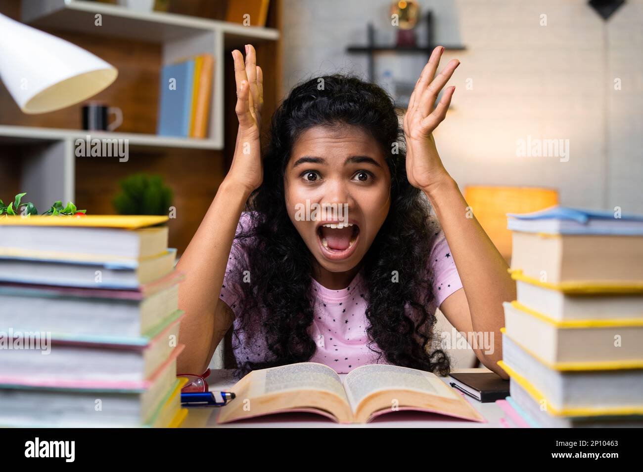 Shouting or screaming young girl in front of stack of books on study ...