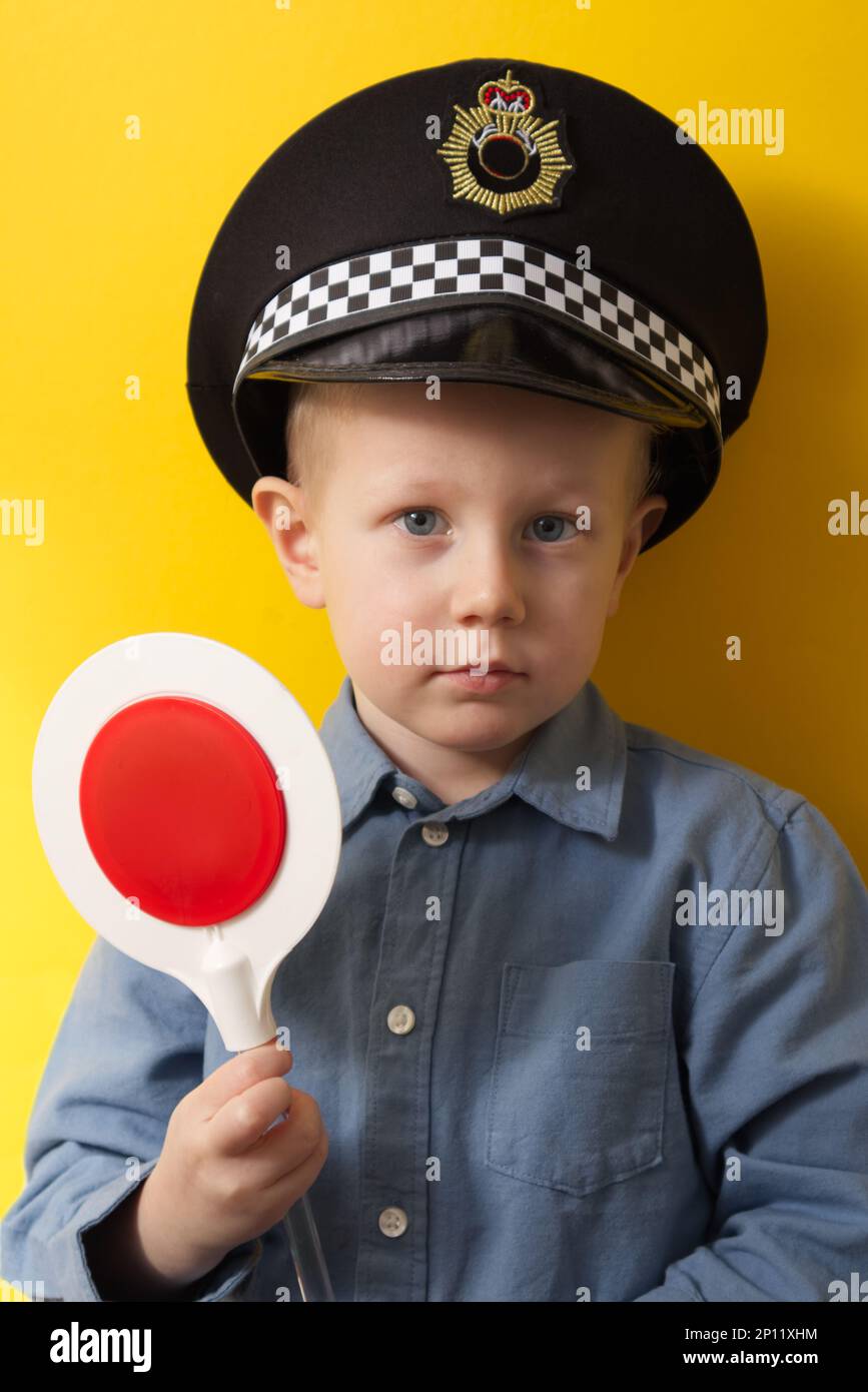 Boy in a cap of a policeman showing a red traffic light on a yellow ...