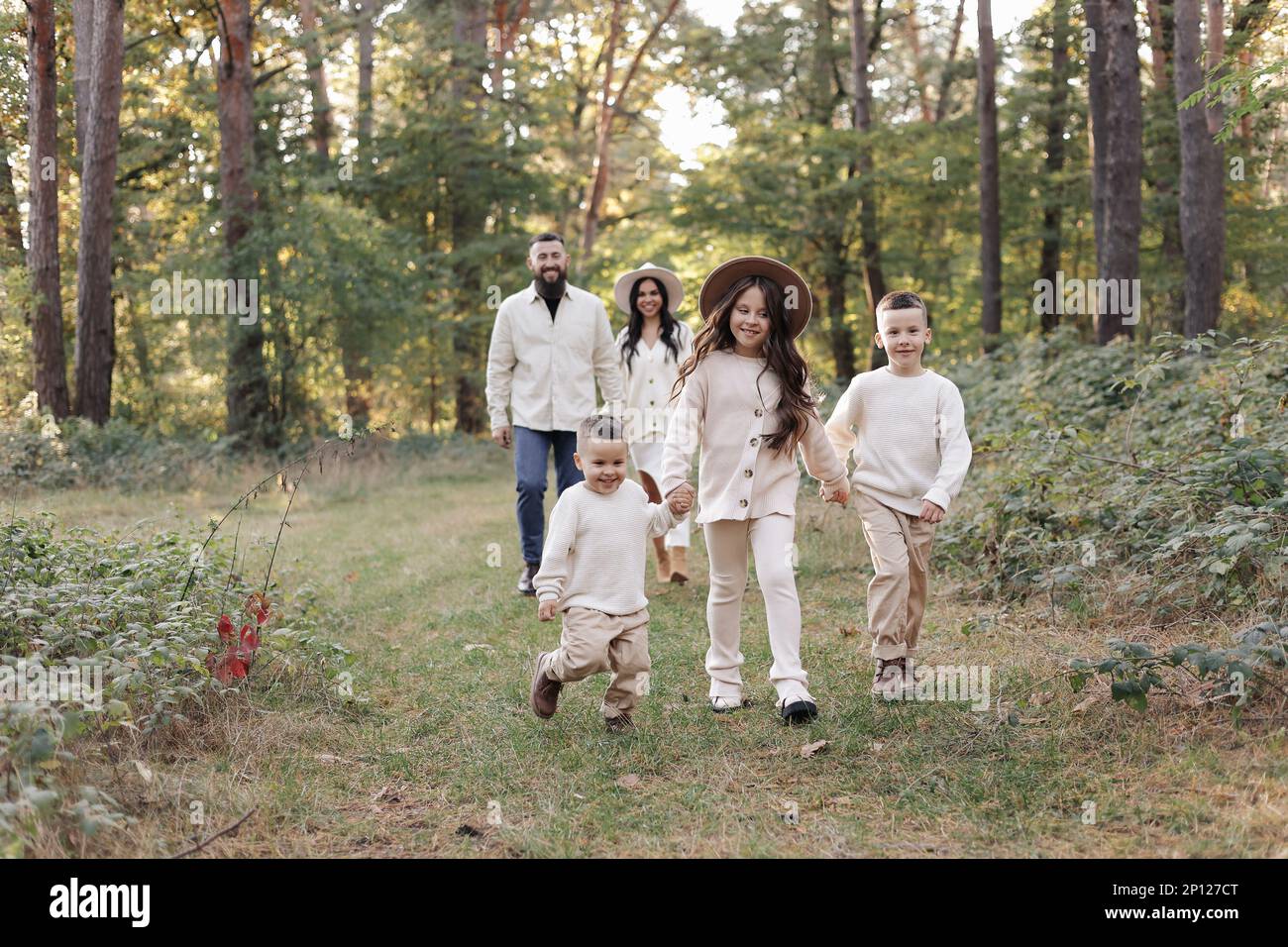 Young mother, father with daughter and sons are walking, having fun in autumn forest. Family ...