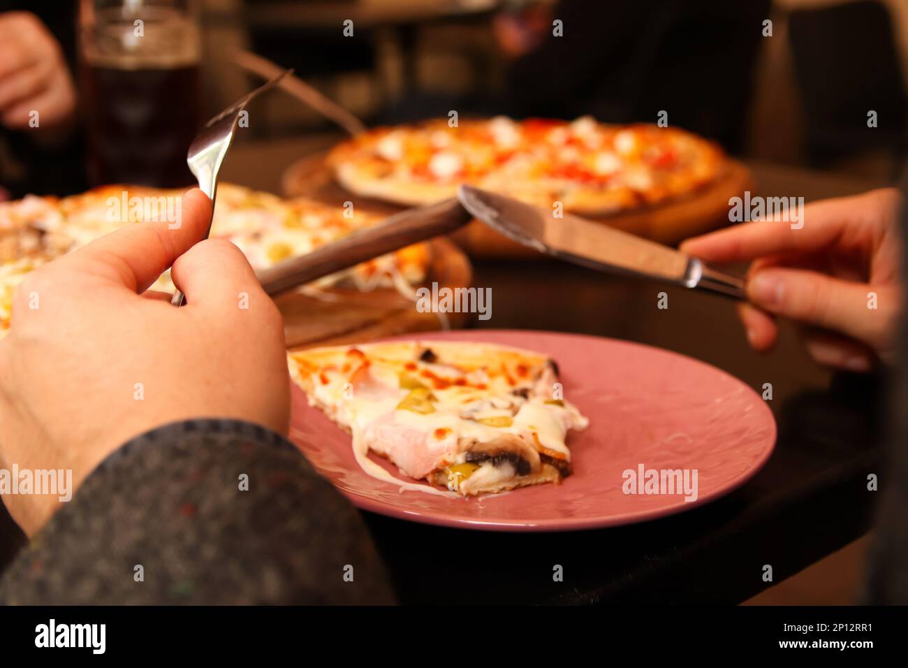 Pizza with knife and fork. Male hand. Defocus person cuts the pizza in ...