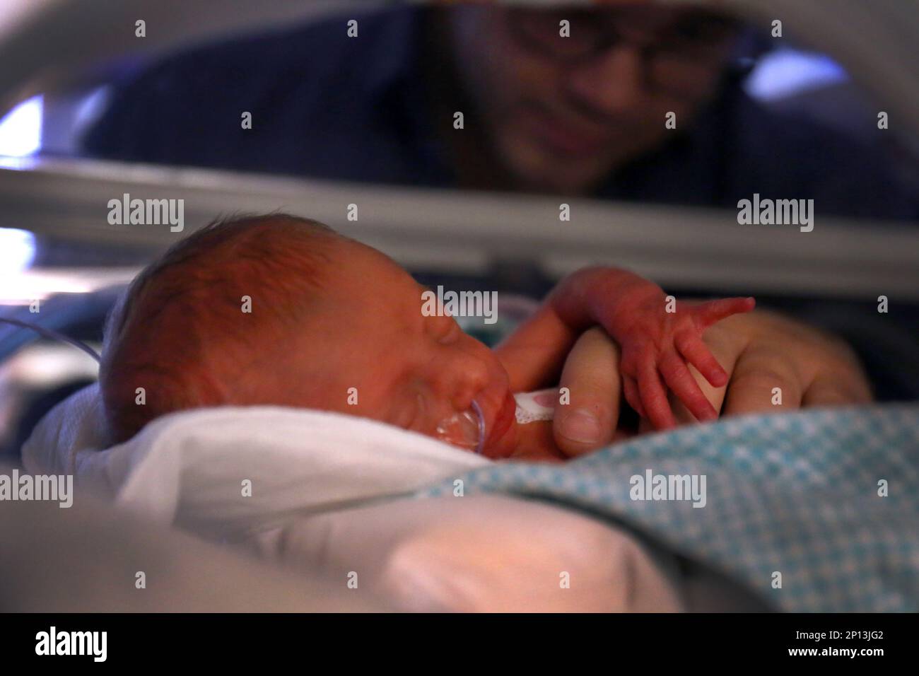 First-born Raelyn stretches in her isolette while her father Logan ...