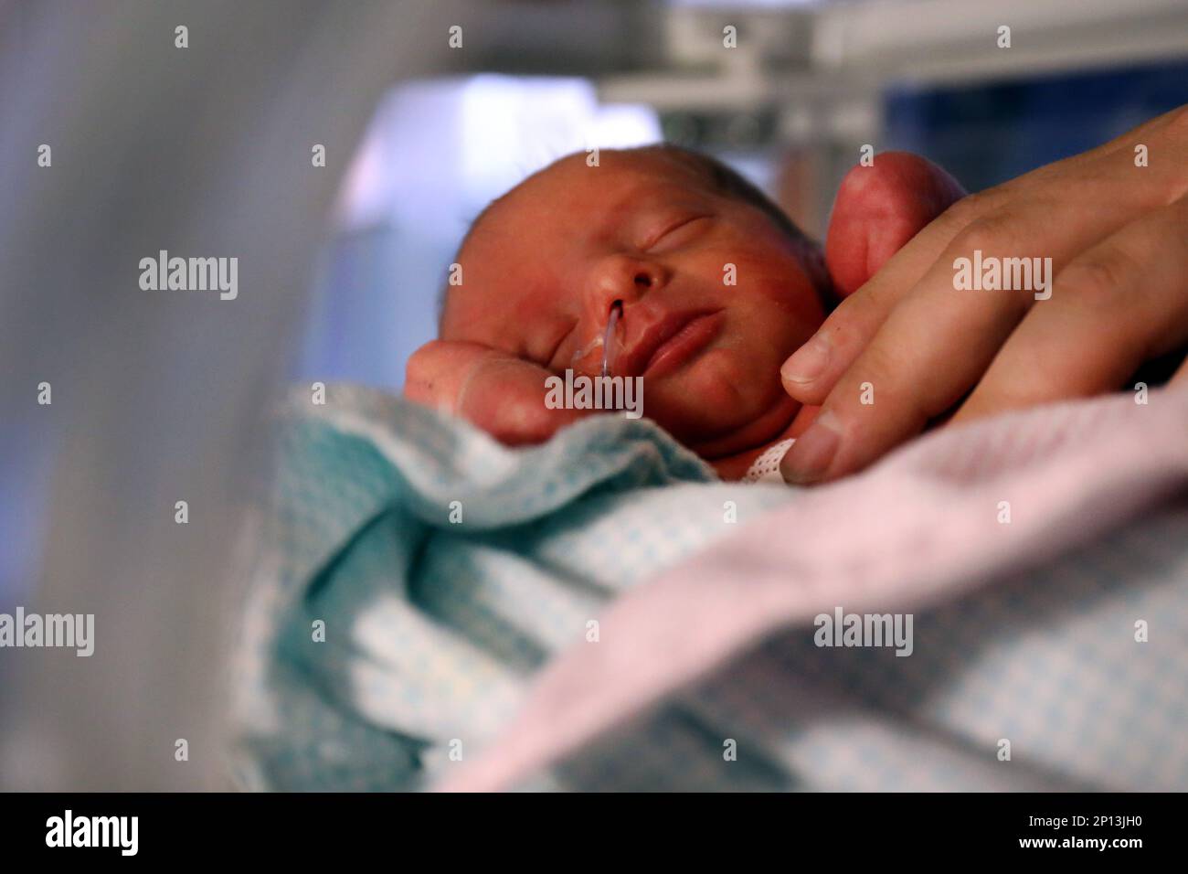 First-born Raelyn stretches in her isolette while her father Logan ...