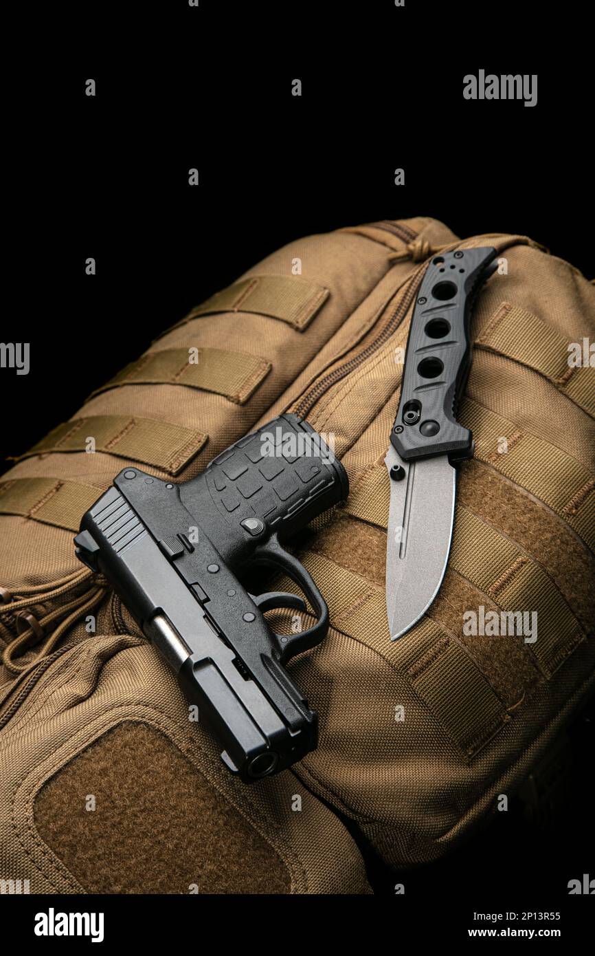 A small modern pistol and penknife on a brown military backpack. Self ...