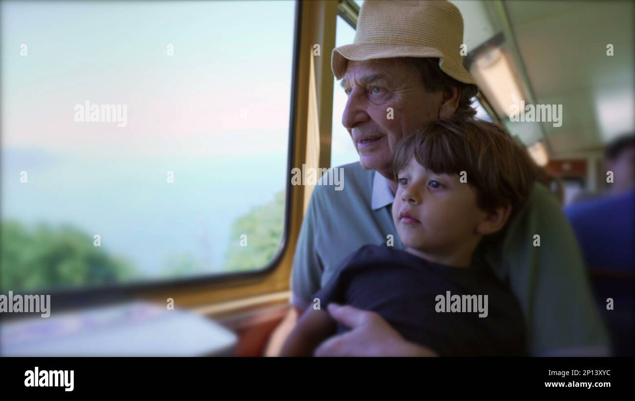 Grandfather and grandson traveling together seated by train window ...