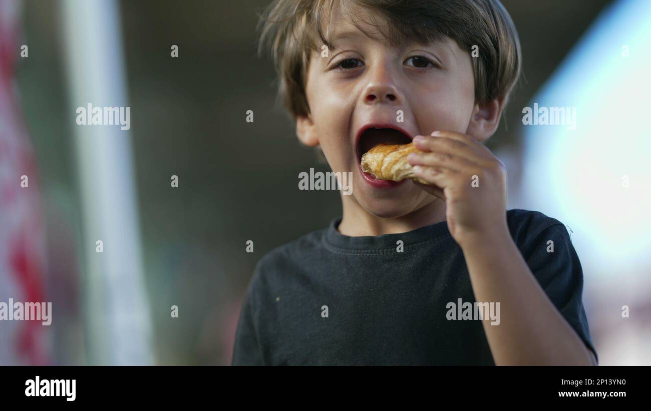 One cute small boy eating piece of bread outside. Child eats snack ...
