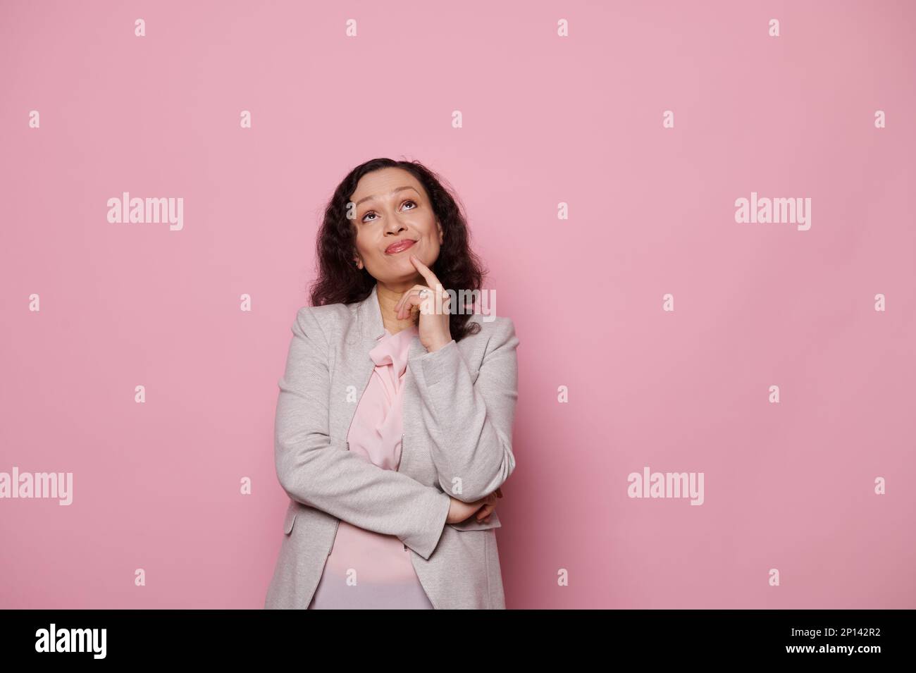 Pensive woman in elegant light gray suit, looking up, reasoning ...