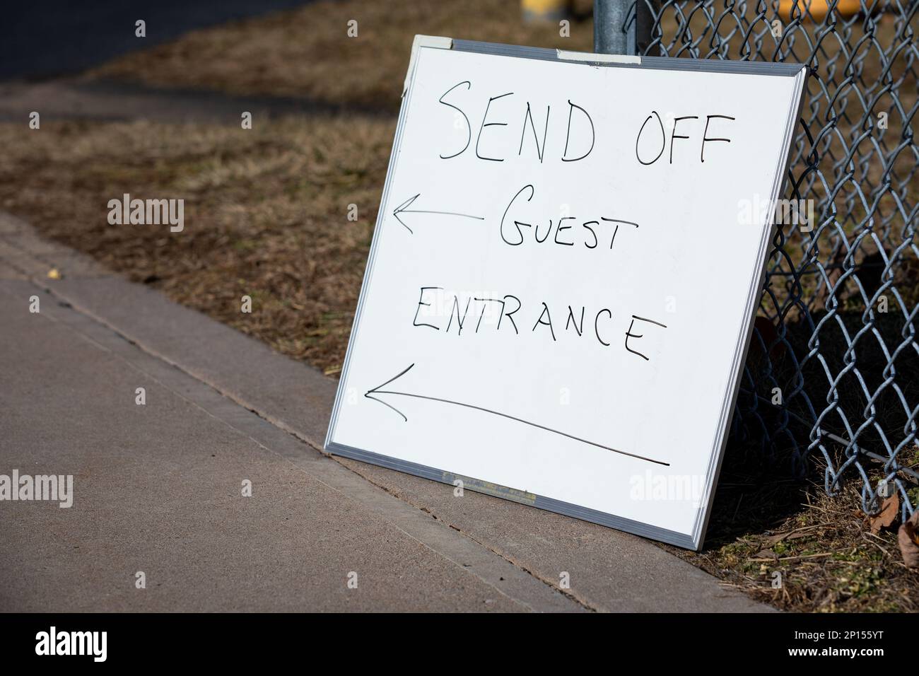 A sign directing guests is placed against a chain link fence outside ...