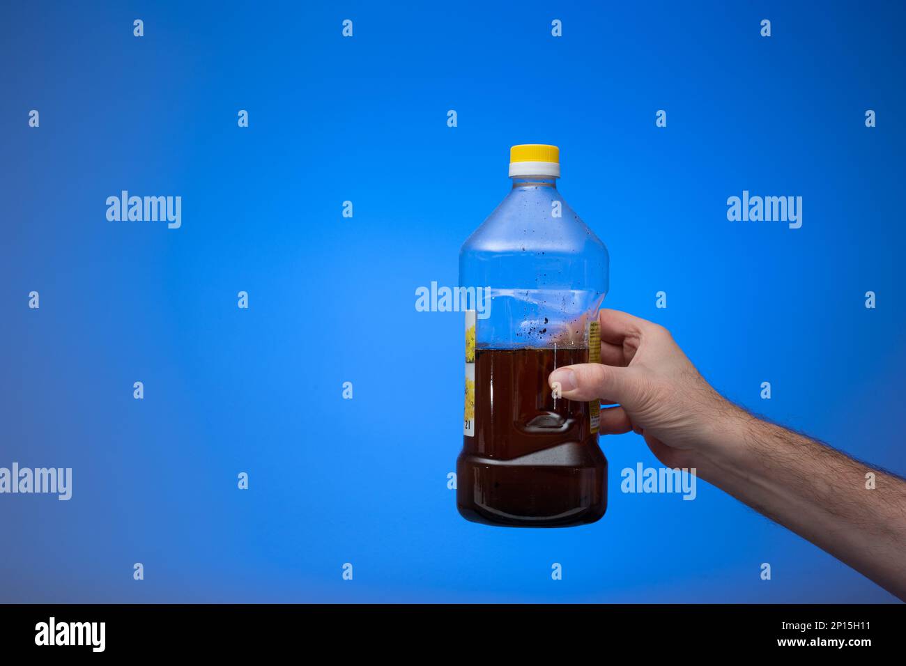 Spent cooking oil recycling in a clear plastic bottle. Held in hand by ...