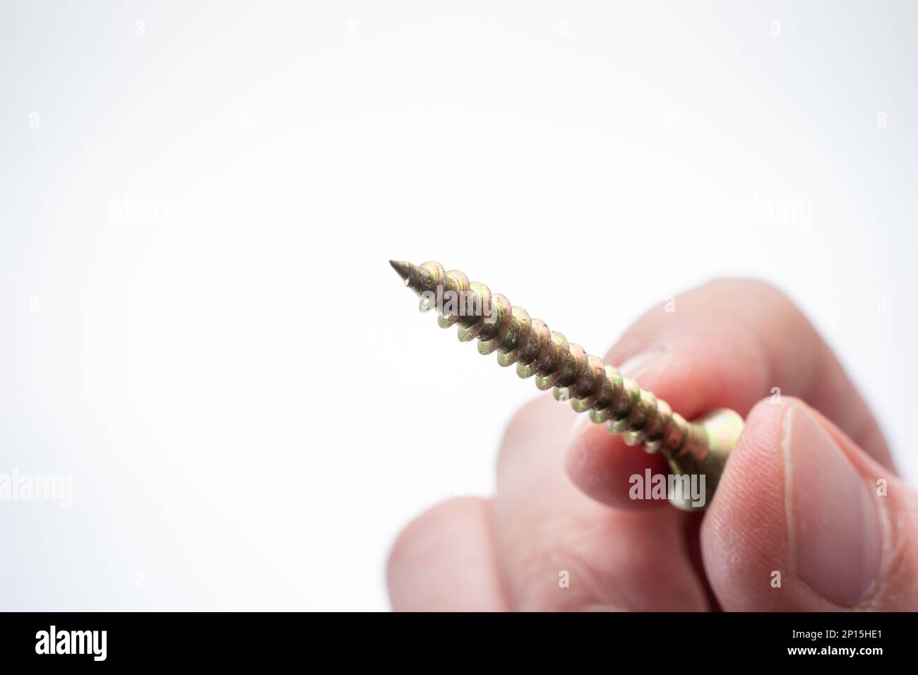Small metal threaded screw held by Caucasian male hand between fingers ...