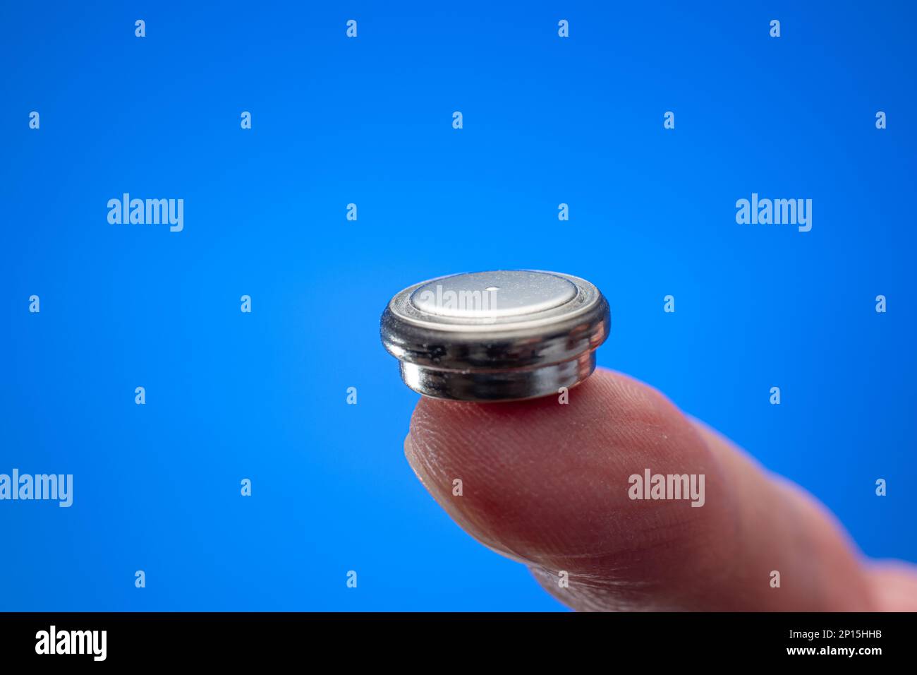 Caucasian male hand holding a button type battery between fingers ...