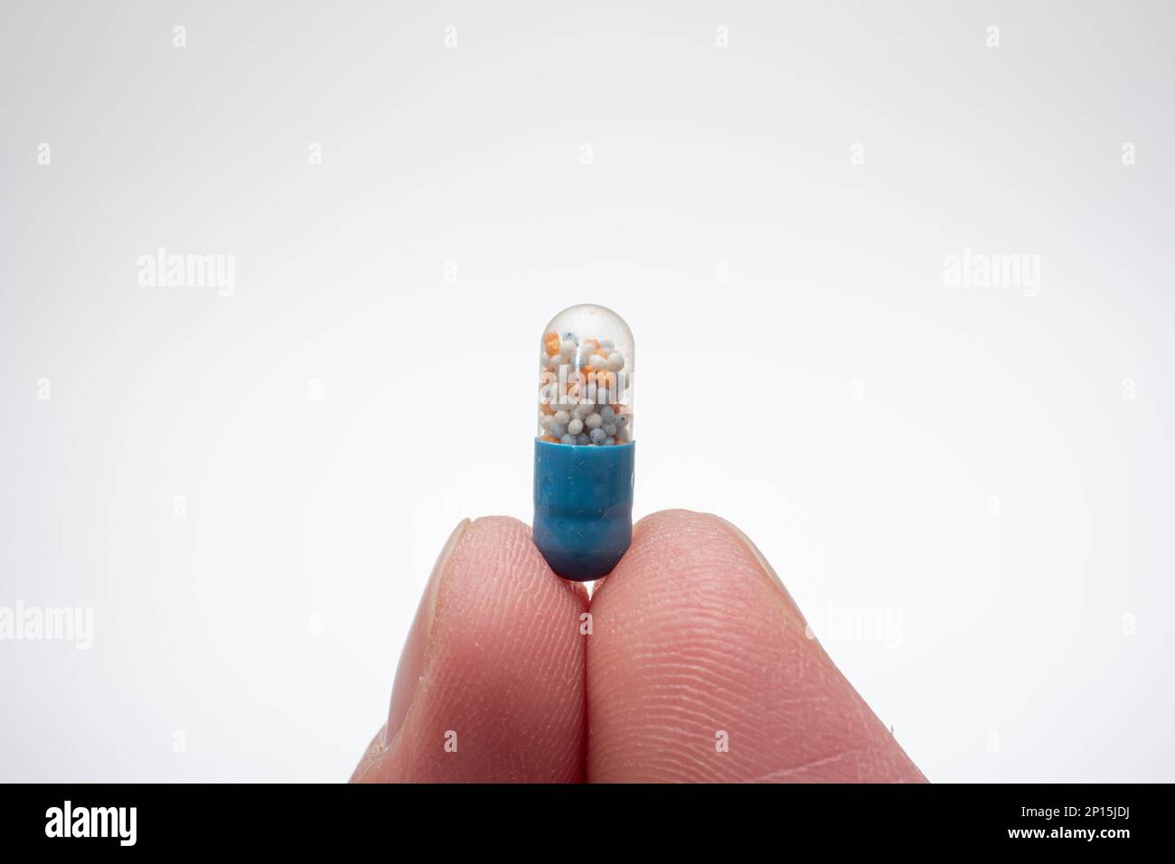Small medicine medicament capsule half blue half transparent held ...