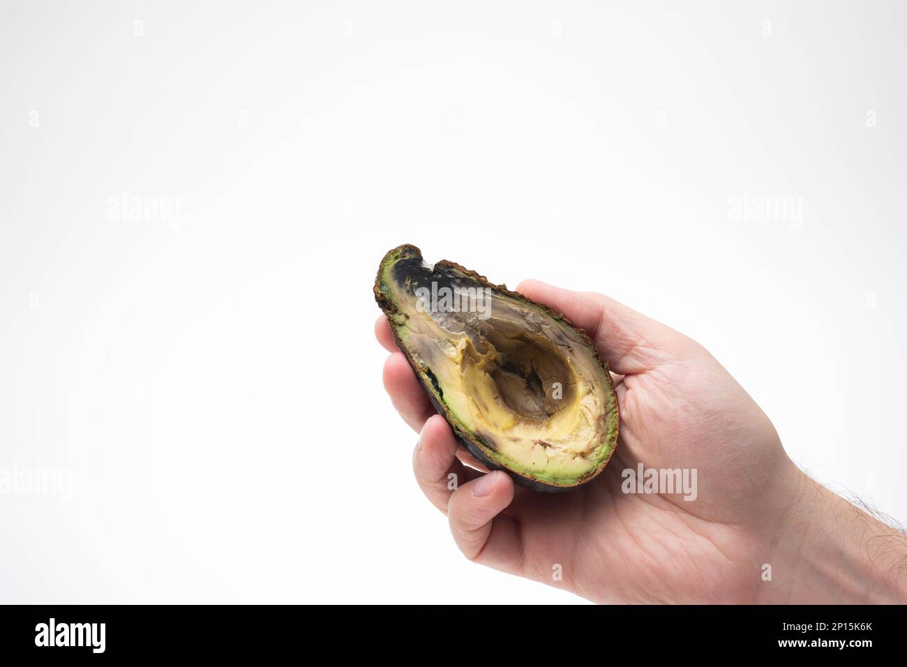 Male hand holding a spoiled rotten overripe avocado fruit cut in half ...