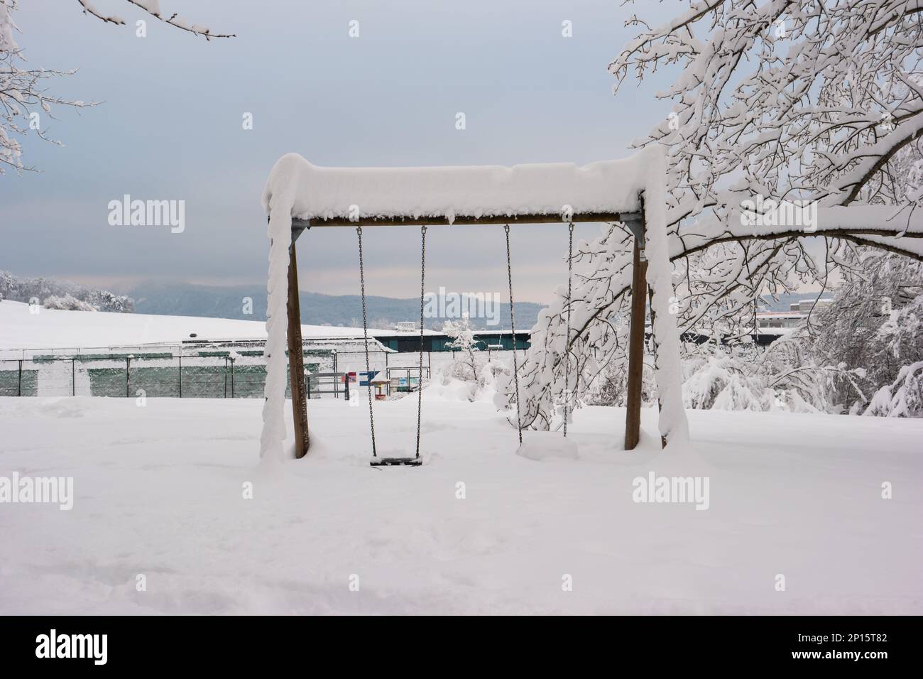 Snowy playground in the forest with snow covered swing and trees in ...