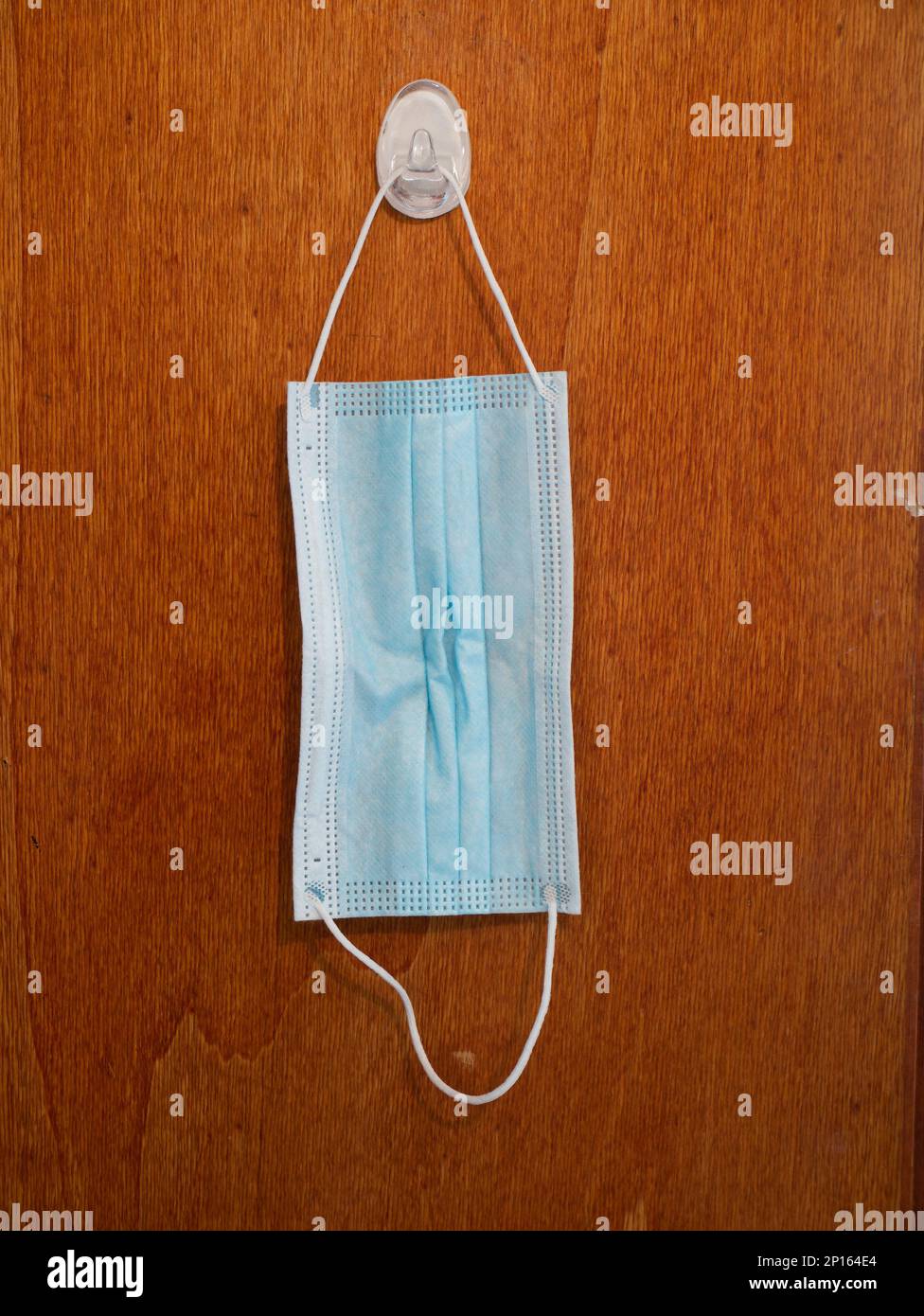Sterile unused blue face mask hanging from a brown wooden door isolated ...