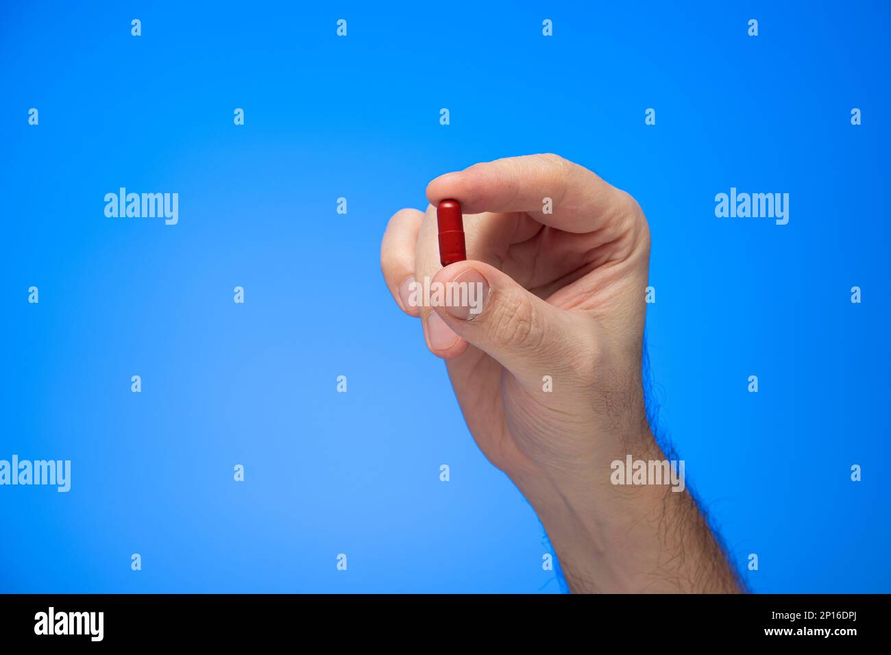 Red capsule medical pill held between fingers by Caucasian male hand ...
