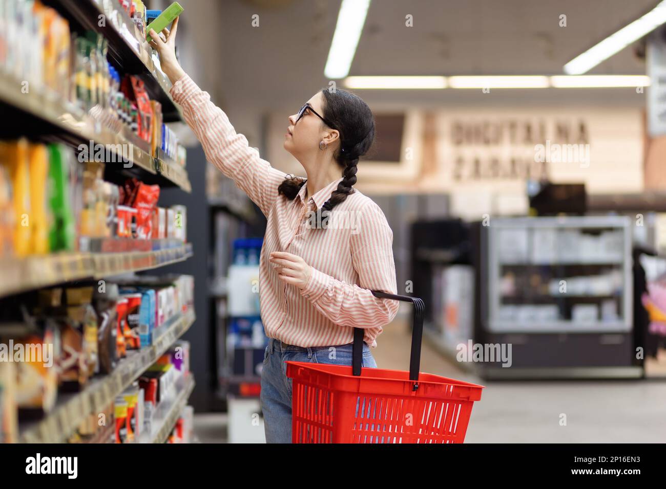 Side view of young Caucasian female student holds basket and reach hand ...