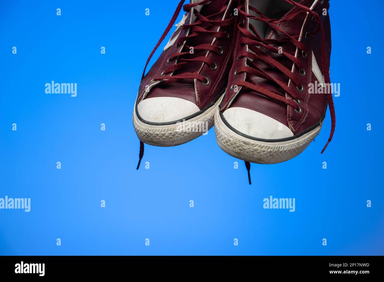 Pair of worn out dirty old red shoes isolated on blue background studio ...