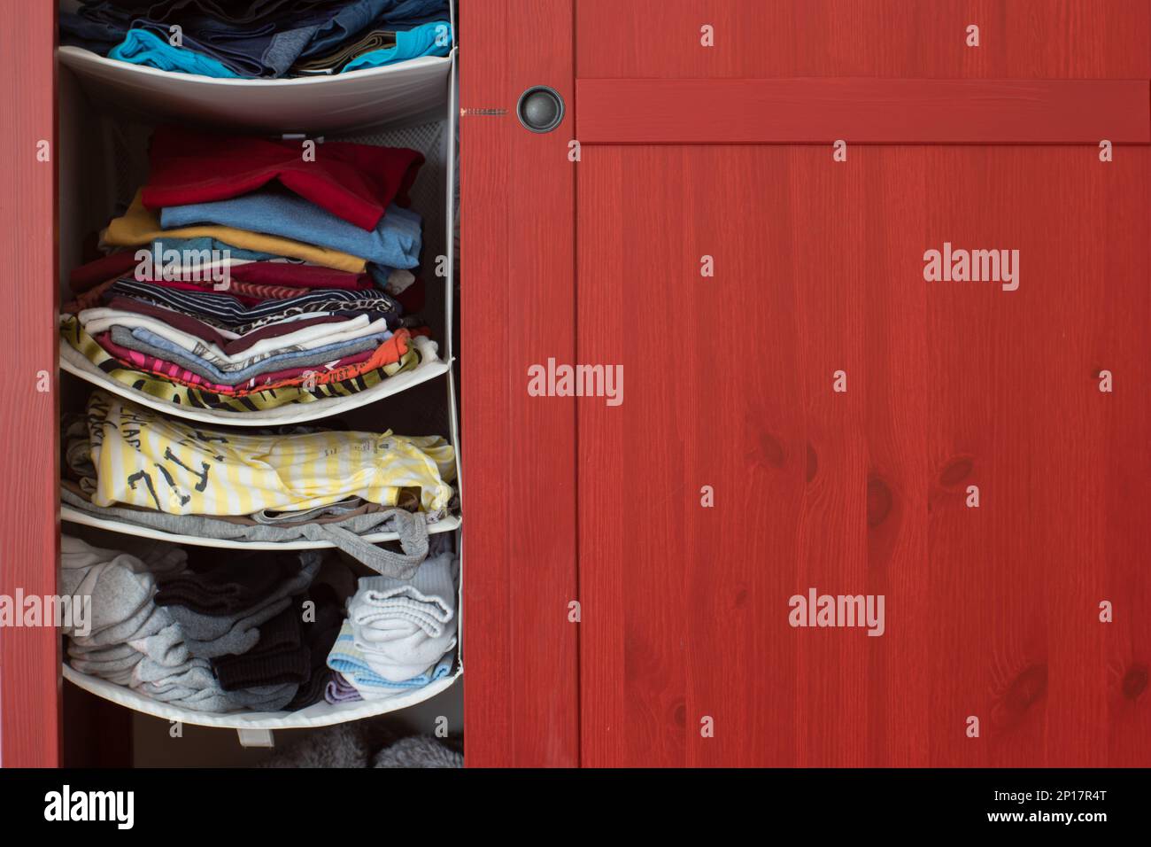 Variety of used folded clothing inside home closet red wooden cupboard ...