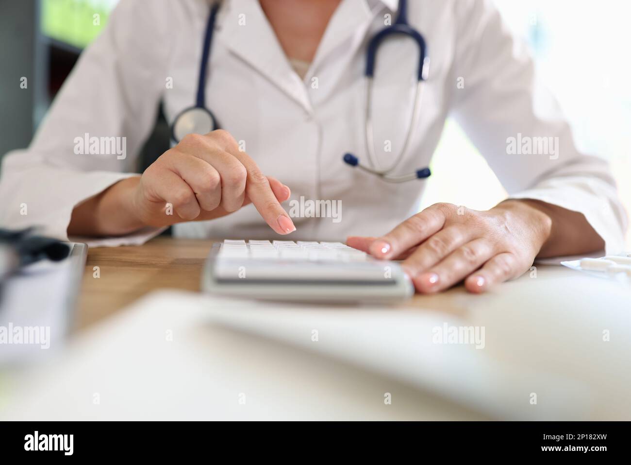 Woman doctor counting on calculator in office Stock Photo - Alamy