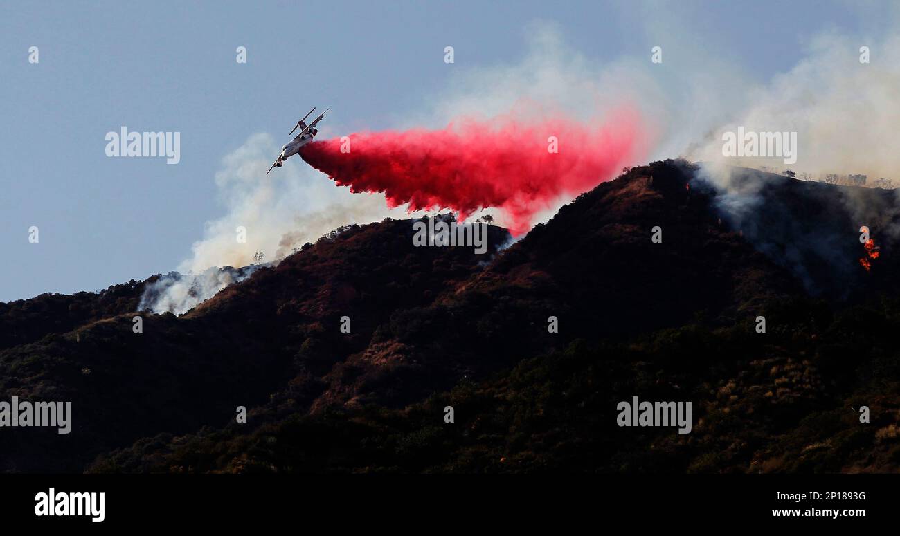 A firefighting plane makes a retardant drop on a hill near a wildfire ...