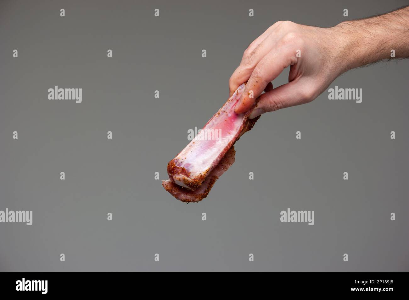 Raw seasoned sliced pork rib held by Caucasian male hand studio shot ...