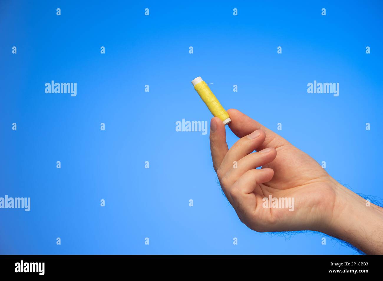 Small reel of yellow sewing thread held in hand by Caucasian male hand ...