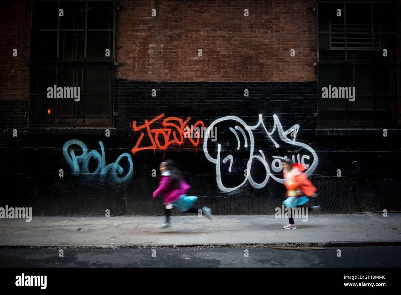Two young girls running in front of graffiti in New York City street ...