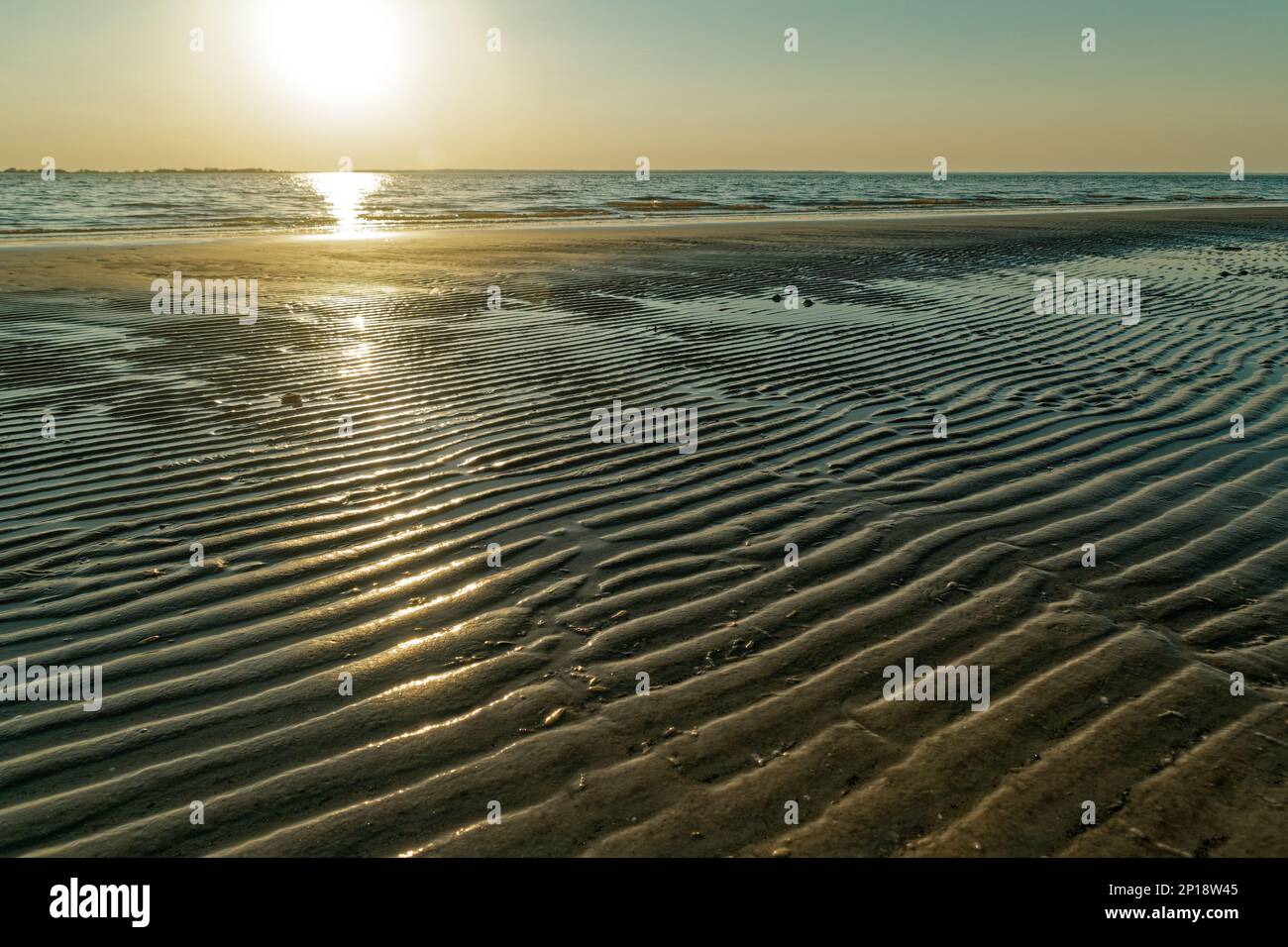 Bright sunlight reflecting across the rippled beach during setting with ...