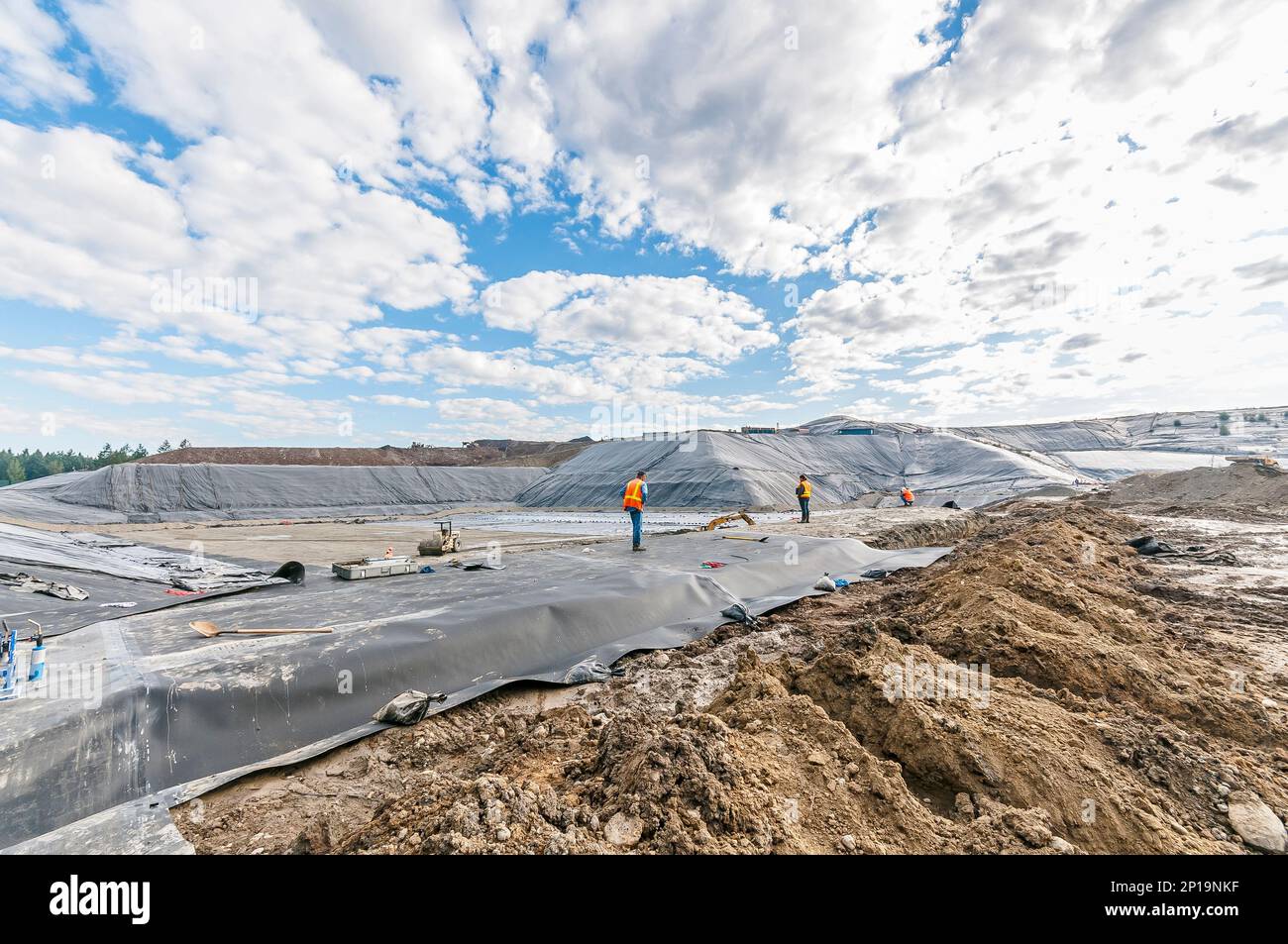 Workers in vast areas of excavation and plastic geomembrane coverings ...