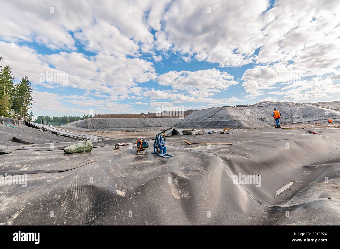 Workers in vast areas of excavation and plastic geomembrane coverings ...