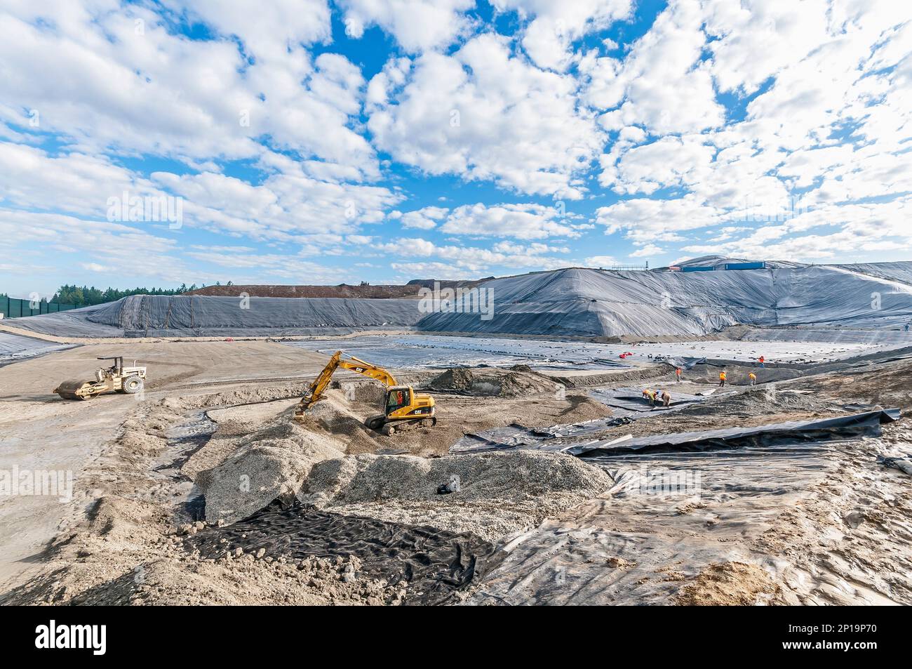 Workers in vast areas of excavation and plastic geomembrane coverings ...