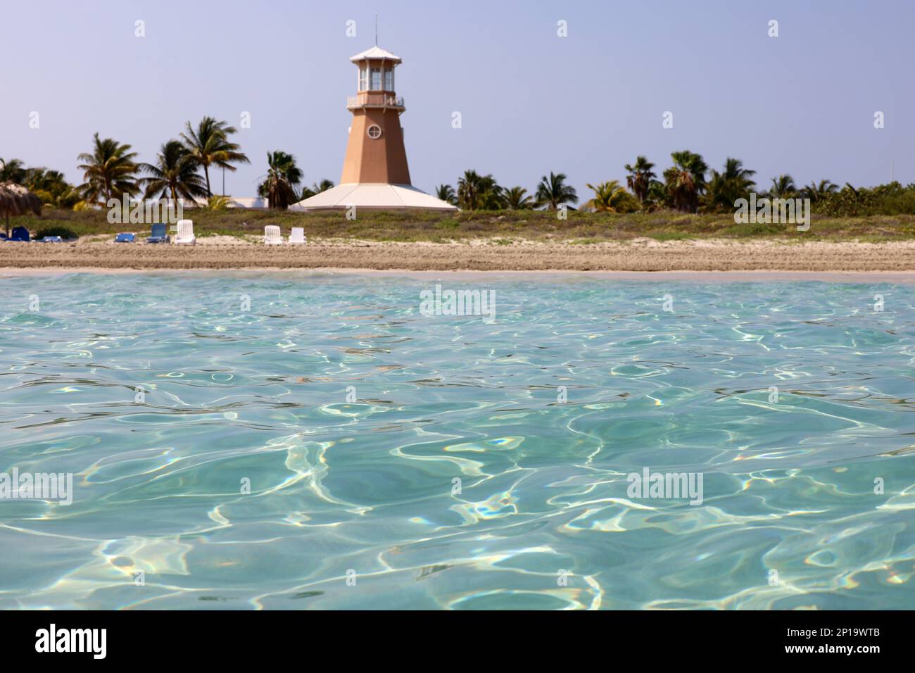 Defocused view from the water surface to tropical beach with lighthouse ...