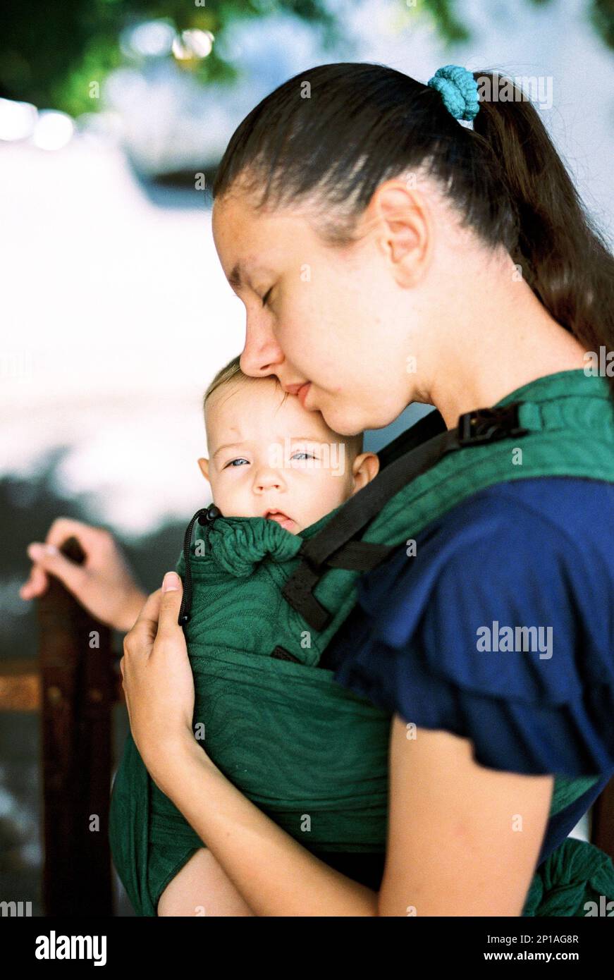 Mom hugging a baby in a baby carrier while standing in the garden Stock ...