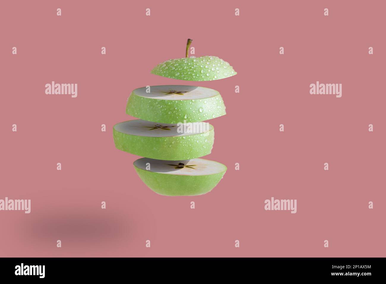 A fresh green apple split into pieces in midair against a pastel ...