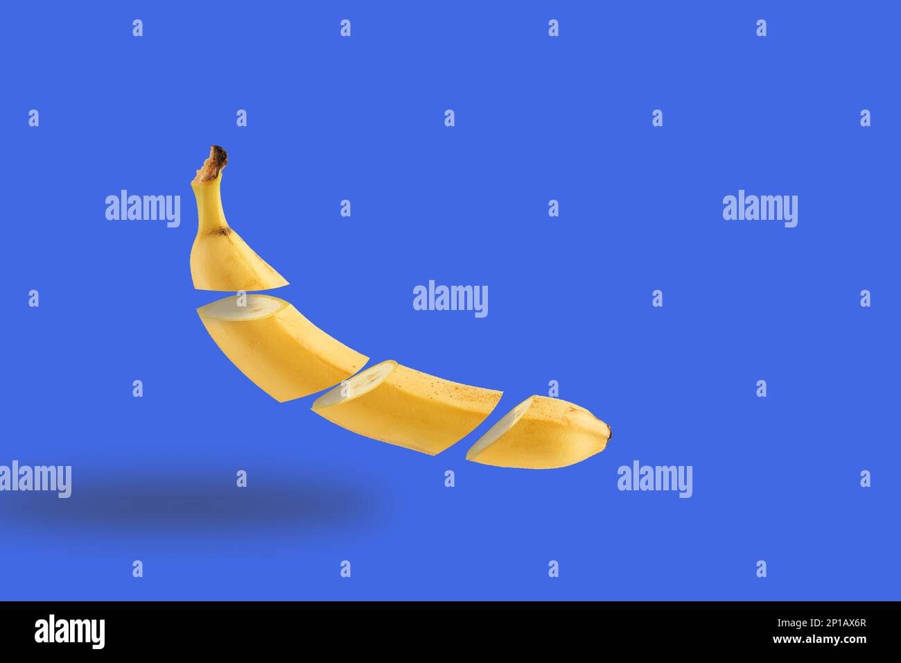 A fresh banana split into pieces in midair against a blue backdrop ...