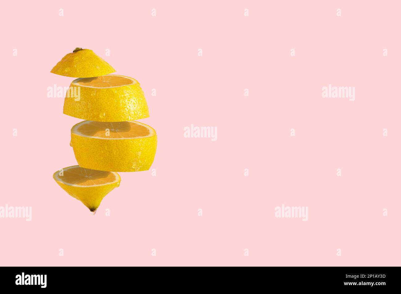 A fresh lemon split into pieces in midair against a pink pastel ...