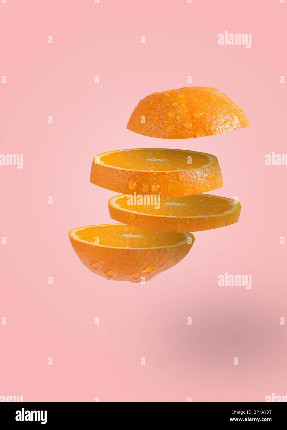 A vertical shot of a fresh orange split into pieces in midair against a ...